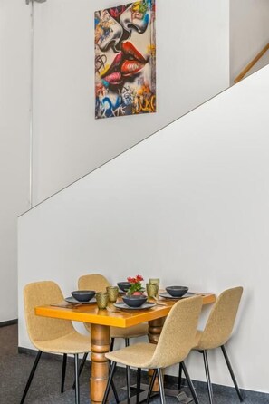 Uma área de refeições com uma mesa posta para quatro pessoas, cadeiras e um quadro abstrato colorido na parede.