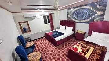 Quarto de hotel com uma cama, uma escrivaninha, uma cadeira e um ventilador de teto.