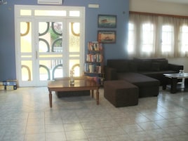 Uma sala de estar com um sofá seccional, uma mesa de centro, uma estante de livros e uma porta com painel de vidro.