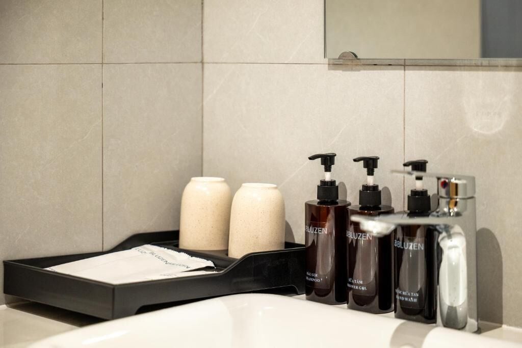 Um banheiro com uma pia, duas garrafas de shampoo, uma garrafa de condicionador e um porta-sabonete com uma toalha branca.