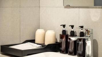 Um banheiro com uma pia, duas garrafas de shampoo, uma garrafa de condicionador e um porta-sabonete com uma toalha branca.