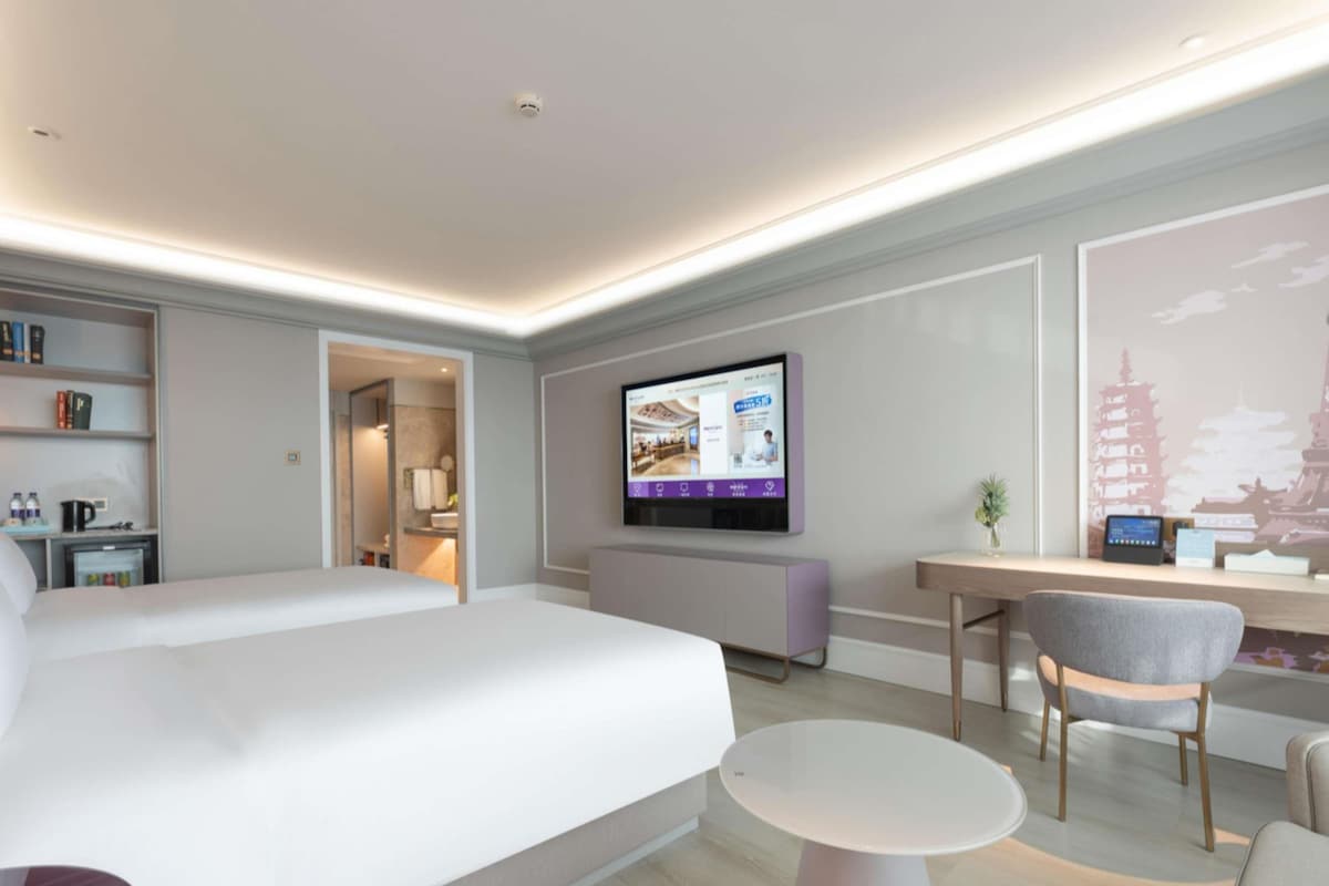 Quarto de hotel moderno com uma cama grande, uma escrivaninha, uma cadeira e uma televisão na parede.