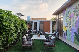 Uma área externa com mesas e cadeiras, um painel solar e um edifício com um mural colorido.