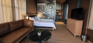 Quarto de hotel com uma cama, um sofá, uma mesinha com uma planta, uma televisão e um armário.