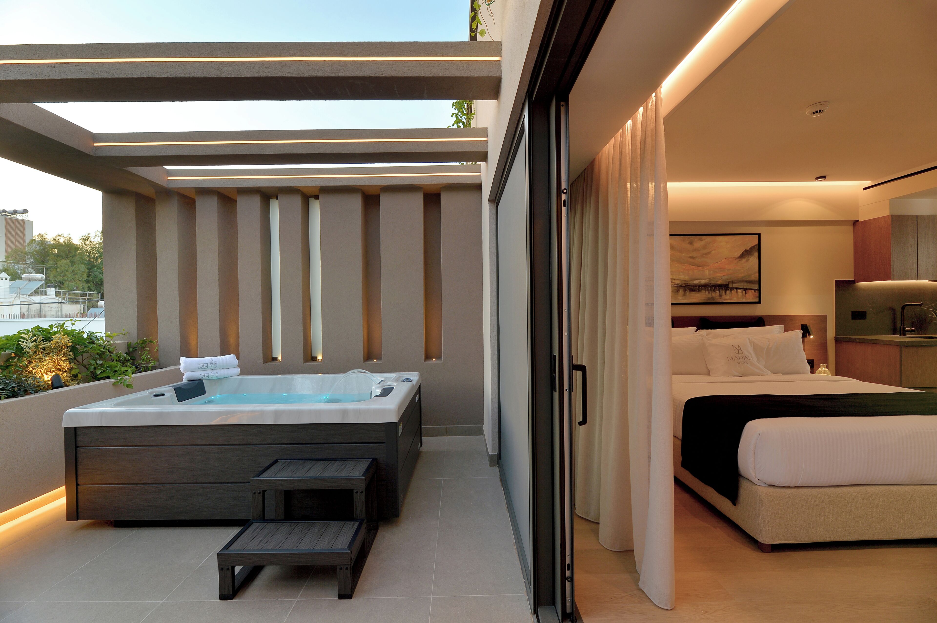 Quarto de hotel moderno com uma cama grande, banheiro com banheira e varanda com hidromassagem e área de estar.