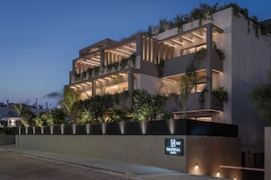 Um hotel com vários andares, varandas, uma placa indicando 'MARINA SUITES' e uma entrada com portão.