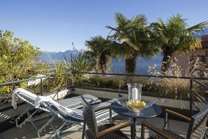 Terraço com mesa e cadeiras, com vista para uma paisagem montanhosa.