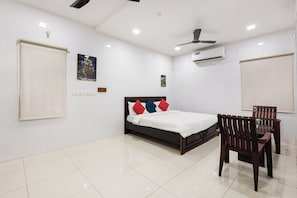 Um quarto com uma cama, um ventilador de teto, um ar condicionado e uma mesa de jantar com cadeiras.