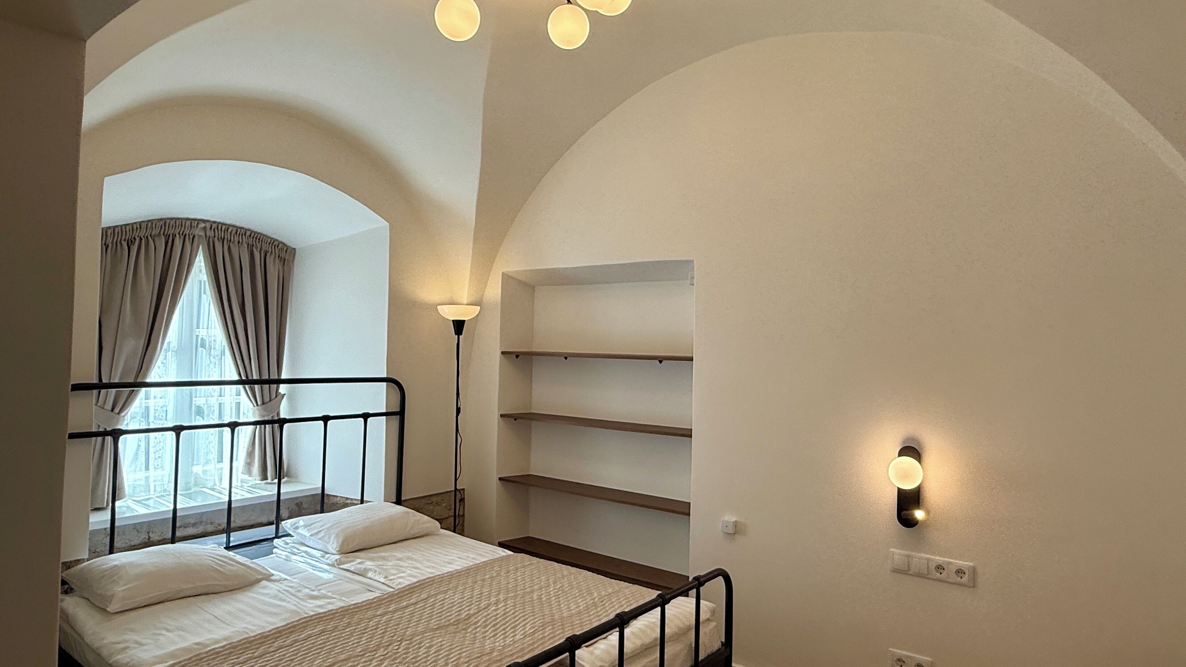 Quarto com cama, mesa de cabeceira, abajur e estante.