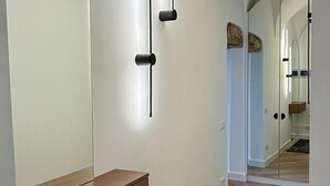 Um corredor com um banco de madeira, um tapete escuro e um candeeiro fixado na parede.