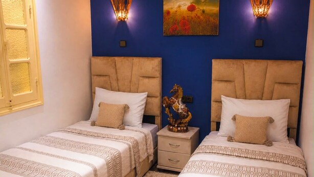 Quarto com duas camas, uma mesa de cabeceira e arandelas decorativas.