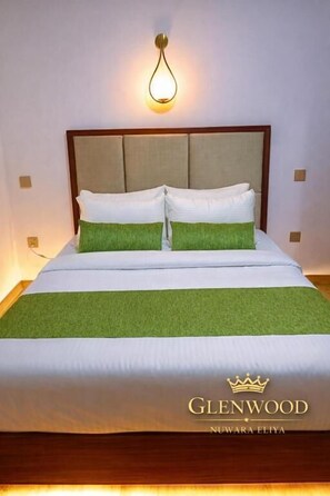 Quarto de hotel com cama, cabeceira e luminária fixada na parede.