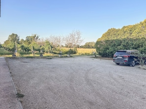 Uma área de estacionamento de cascalho com um carro estacionado, cercada por árvores e vegetação.