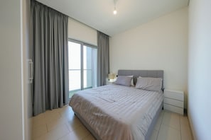 Quarto moderno com uma cama grande, mesa de cabeceira, luminária e janela com cortinas.