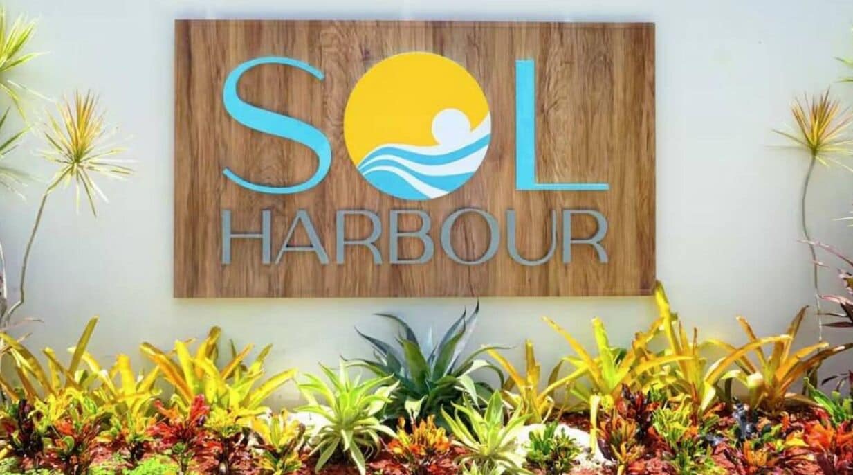 Uma placa de madeira com o texto 'SOL HARBOUR' e um logotipo com um sol e ondas.