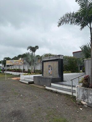 Uma área pavimentada com uma estrutura de concreto, guarda-corpo de metal e um cartaz na parede.