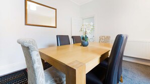 Uma sala de conferências com uma mesa de madeira, seis cadeiras, um vaso com flores e um quadro na parede.