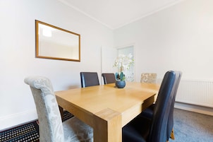 Uma sala de conferências com uma mesa de madeira, seis cadeiras, um vaso com flores e um quadro na parede.