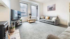 Uma sala de estar moderna com televisão de tela plana, um sofá cinza e uma mesa de centro.