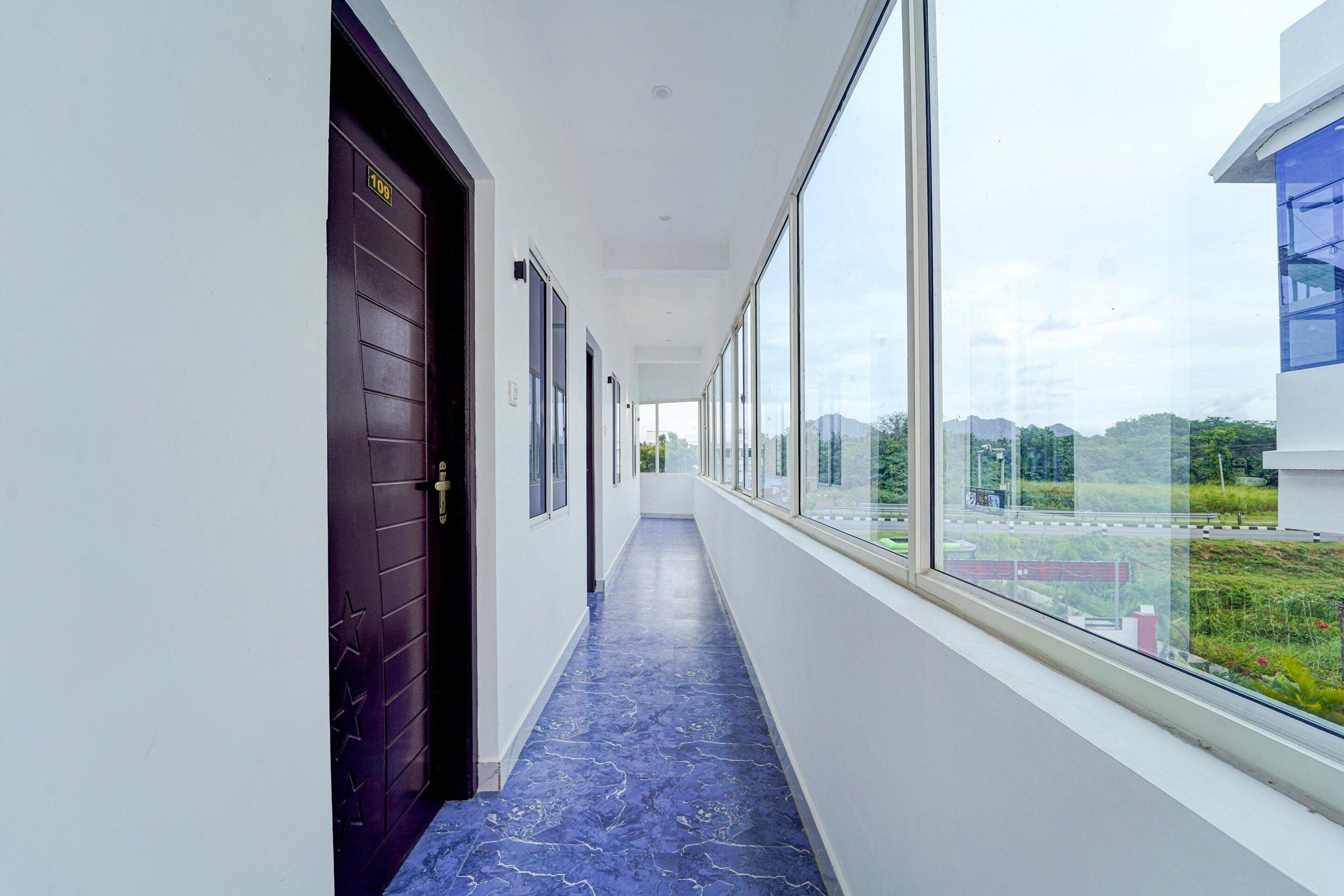 Um corredor com piso de mármore azul, grandes janelas e uma porta com o número 109.