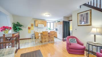 Uma sala de estar ampla com piso de madeira, uma mesa de jantar e uma cozinha ao fundo.