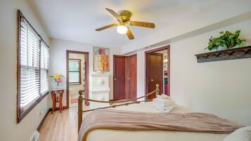 Quarto com cama, ventilador de teto, cômoda, espelho e janela com persianas.