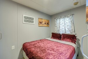 Quarto com cama, janela com cortinas, ventilação por ar condicionado na parede e um quadro.