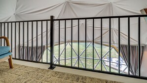 Uma tenda com um corrimão de metal, uma cadeira de madeira e vista para o exterior.