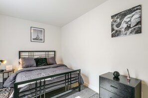 Quarto minimalista com cama, mesa de cabeceira e cômoda.