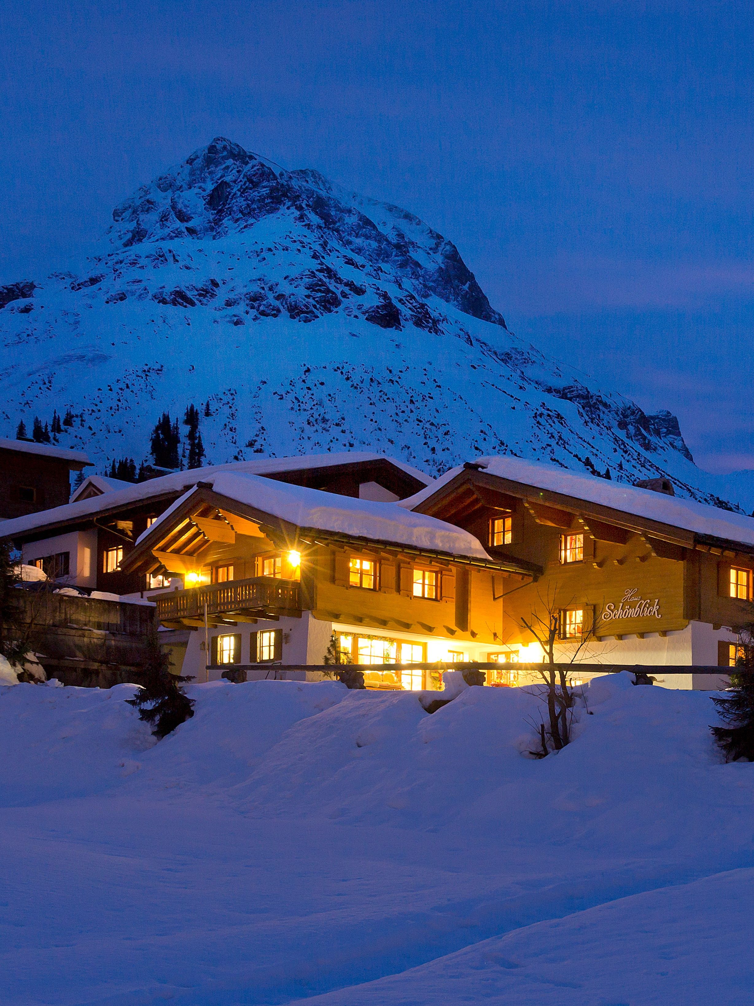 Montanha coberta de neve ao entardecer com um hotel com várias divisões e uma varanda.
