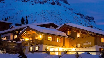 Montanha coberta de neve ao entardecer com um hotel com várias divisões e uma varanda.
