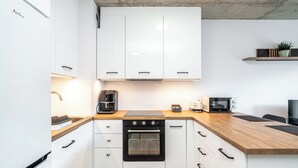 Uma cozinha moderna com armários brancos, bancada de madeira, forno embutido, máquina de café e micro-ondas.