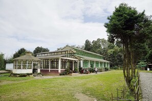 Uma estufa com cobertura de vidro, rodeada por um gramado e árvores.