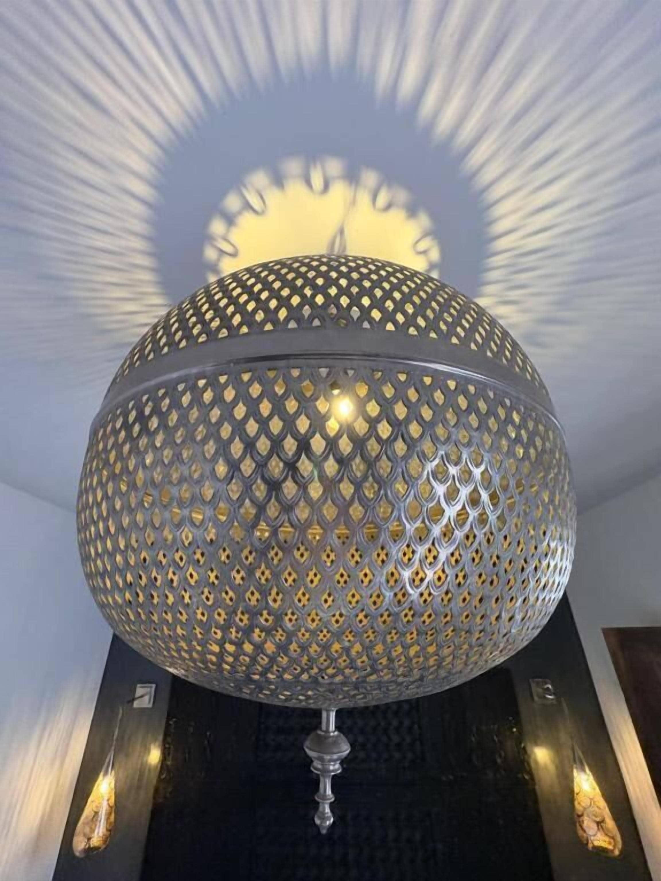Um candelabro esférico com design padronizado, pendurado em um teto com uma luminária circular ao fundo.