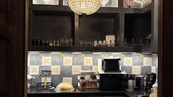 Uma cozinha com um candelabro, prateleiras com copos de vidro, uma cafeteira e um painel de fundo padronizado.