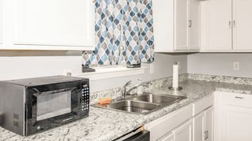 Cozinha com armários brancos, pia de aço inoxidável, micro-ondas e janela com cortinas estampadas.