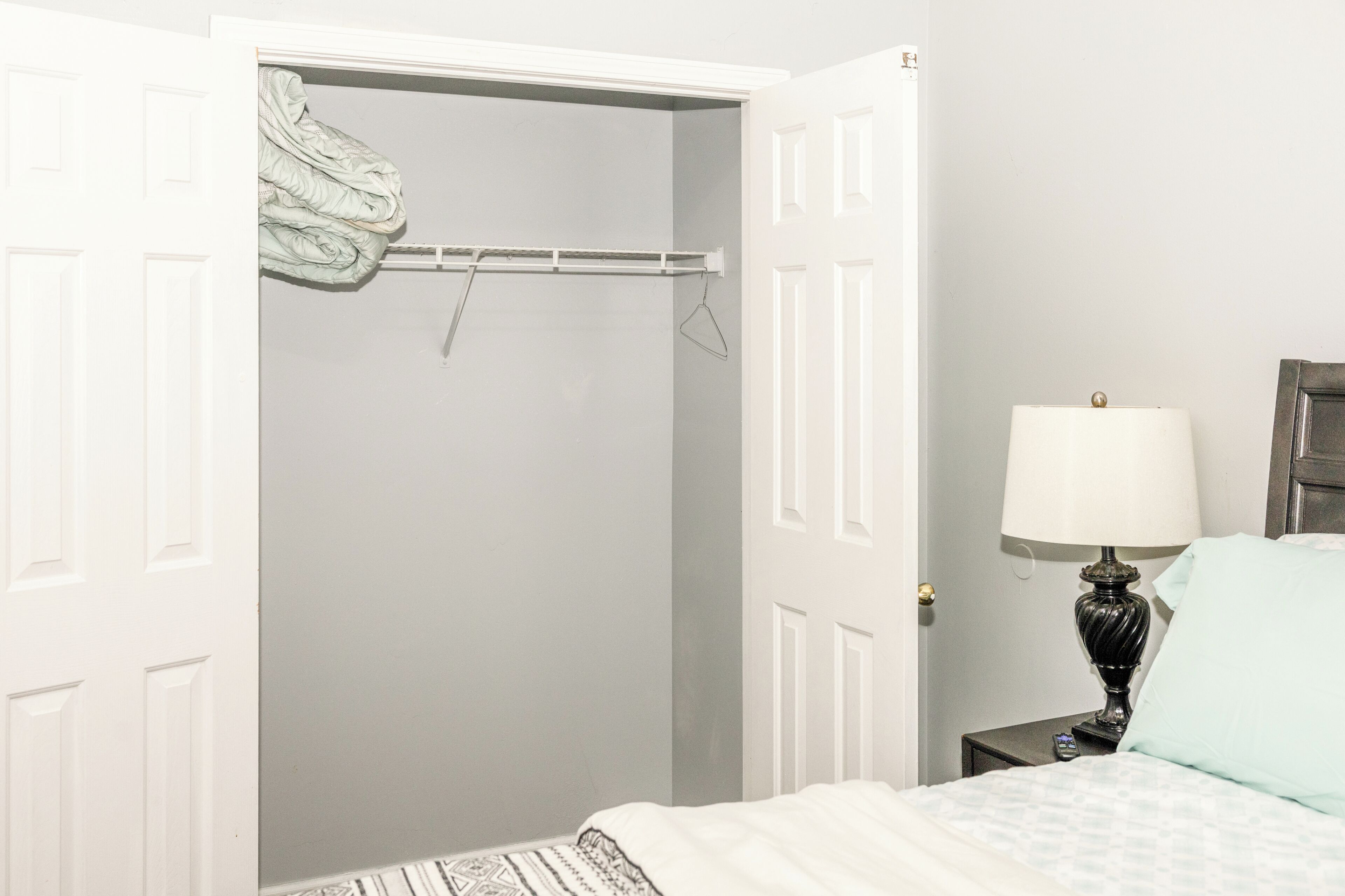Quarto com uma cama, uma mesinha de cabeceira com abajur, um criado-mudo e um armário com cabides.