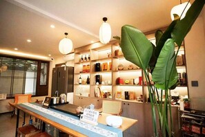 Interior de restaurante com balcão, prateleiras com garrafas e uma planta grande.