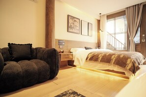 Quarto de hotel com cama, sofá, mesa de cabeceira e janela com cortinas.