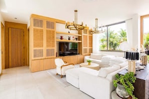 Uma sala de estar moderna com um sofá modular, uma televisão e uma grande janela com vista para palmeiras.