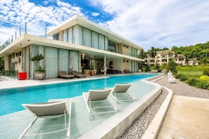 Um hotel moderno com piscina, espreguiçadeiras e área de estar coberta ao ar livre.