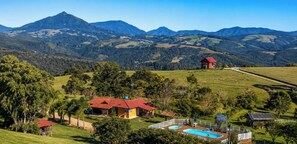 Um estabelecimento com piscina, um edifício com telhado vermelho e vista para montanhas ao longe.