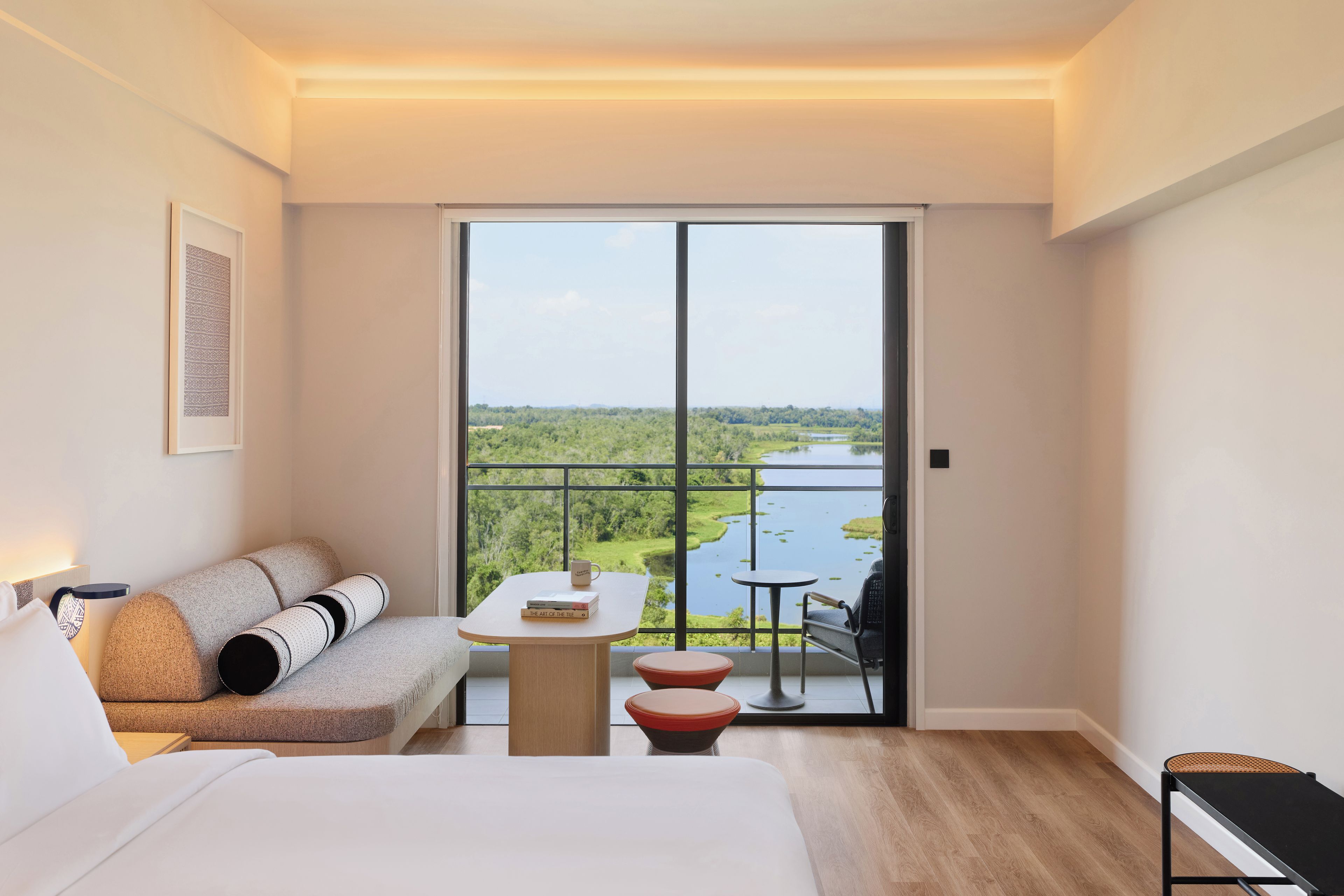 Quarto de hotel moderno com uma grande porta de vidro deslizante que dá para uma varanda com vista para um lago e uma floresta.