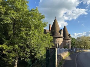 Um edifício de pedra com vários telhados cônicos, rodeado por árvores e uma vedação de metal.