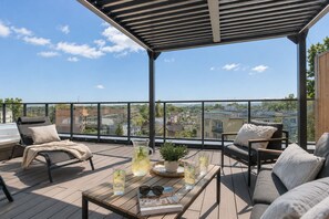 Terraço no telhado com deck de madeira, área de estar ao ar livre, mesa com bebidas e vista para a cidade.