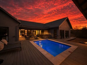 Uma casa moderna com piscina, área de estar externa e céu ao pôr do sol.