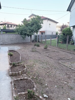 Um jardim com canteiros elevados, uma árvore e uma cerca.