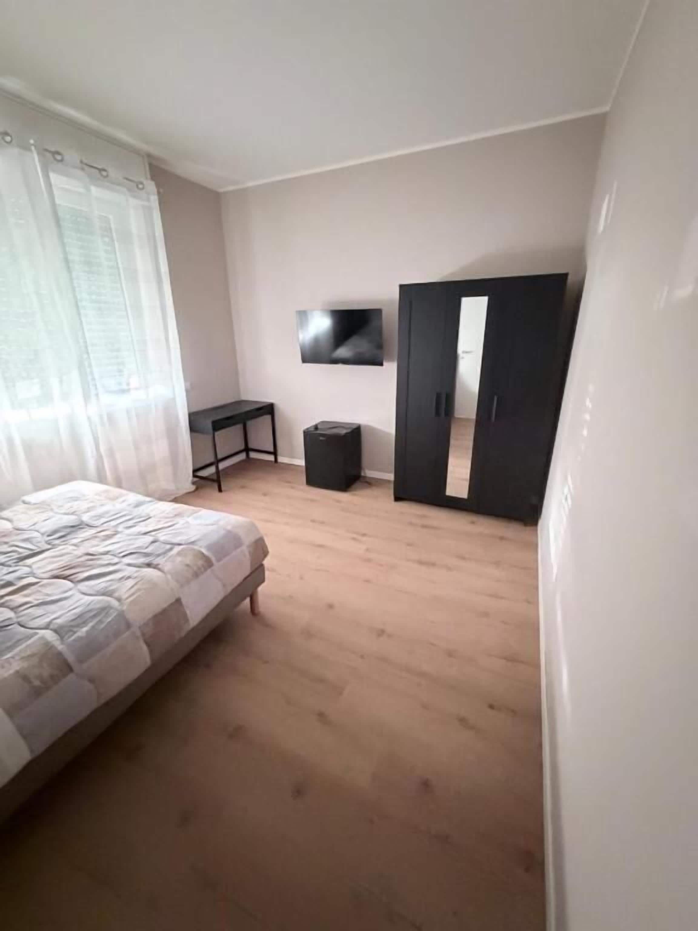 Um quarto com cama, uma mesinha, televisão e guarda-roupa.