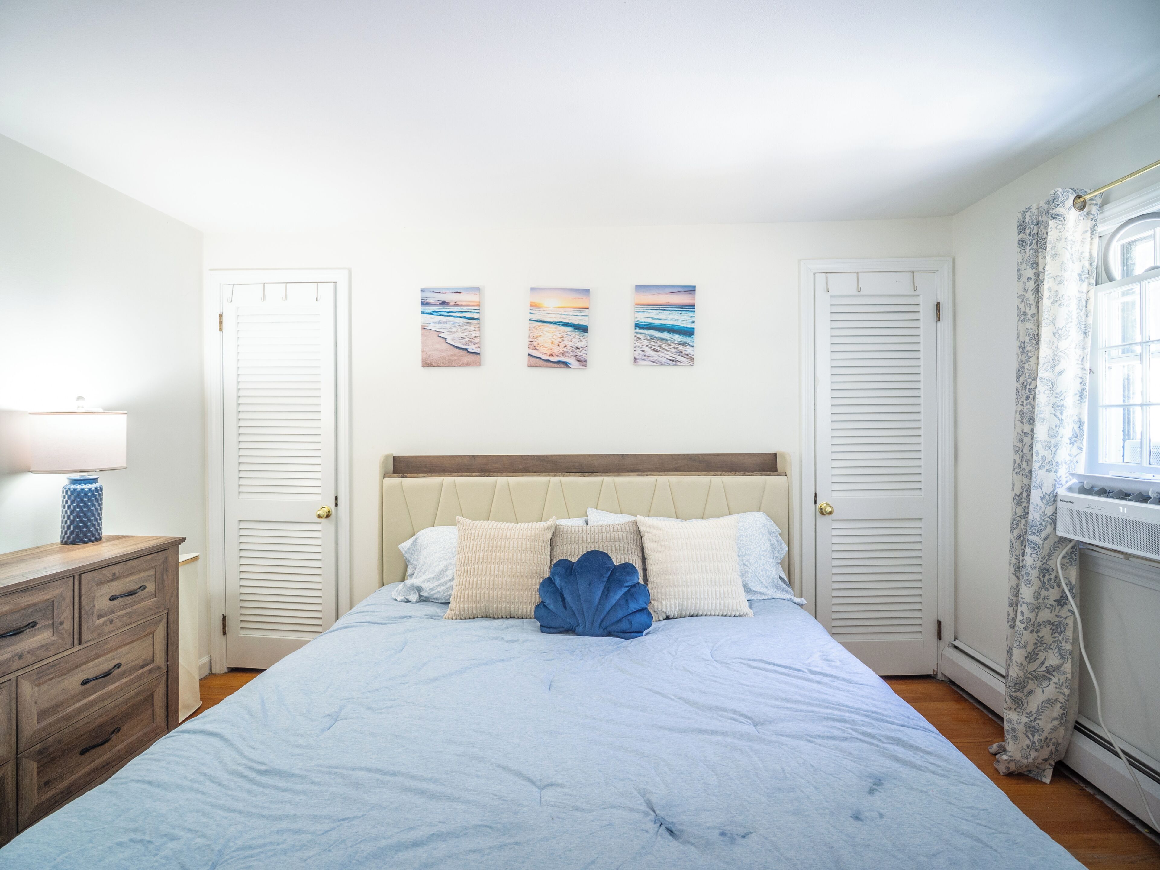 Quarto com cama, penteadeira, janela com cortinas e decoração na parede.