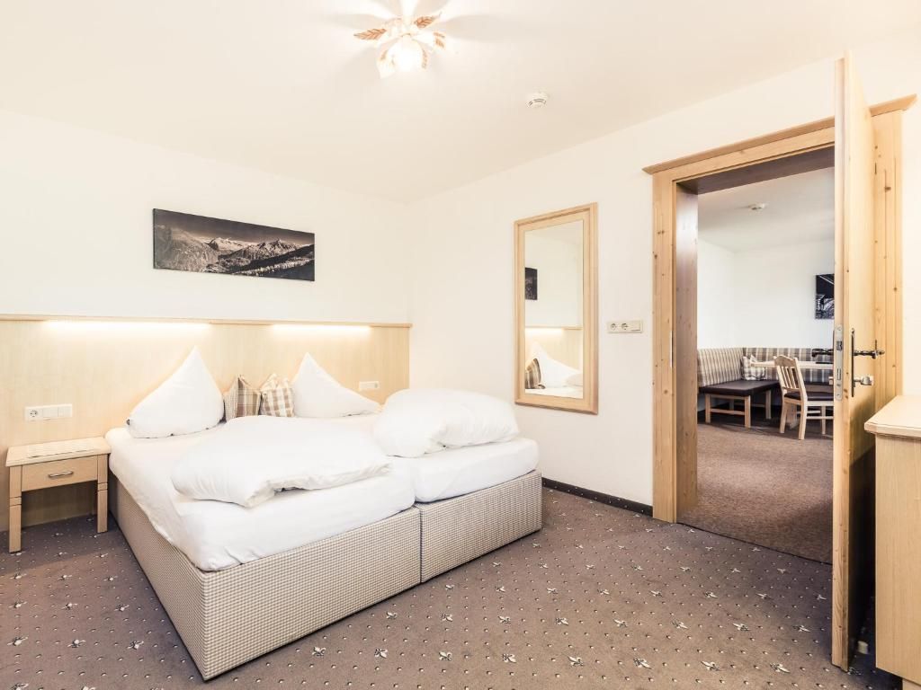 Quarto de hotel com cama, mesa de cabeceira, espelho e porta que dá para uma sala de jantar.